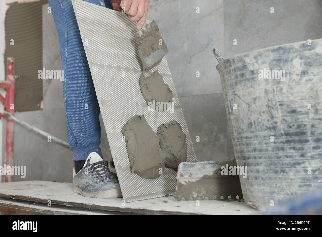 Worker applying cement on wall tile for installation indoors, closeup ...
