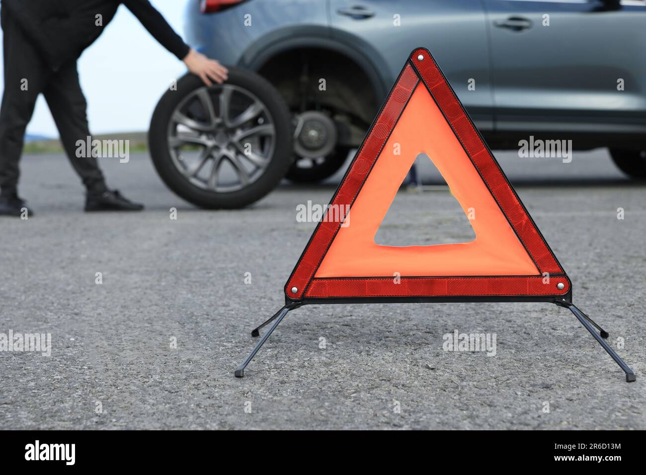 Man changing car tire near road, focus on emergency warning triangle ...