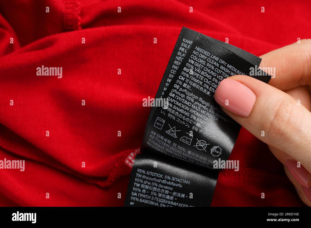 Woman holding clothing labels on red garment, closeup. Space for text ...