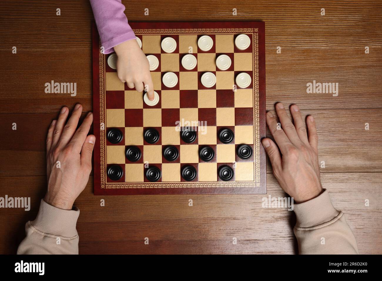 Man playing checkers with child at wooden table, top view Stock Photo ...