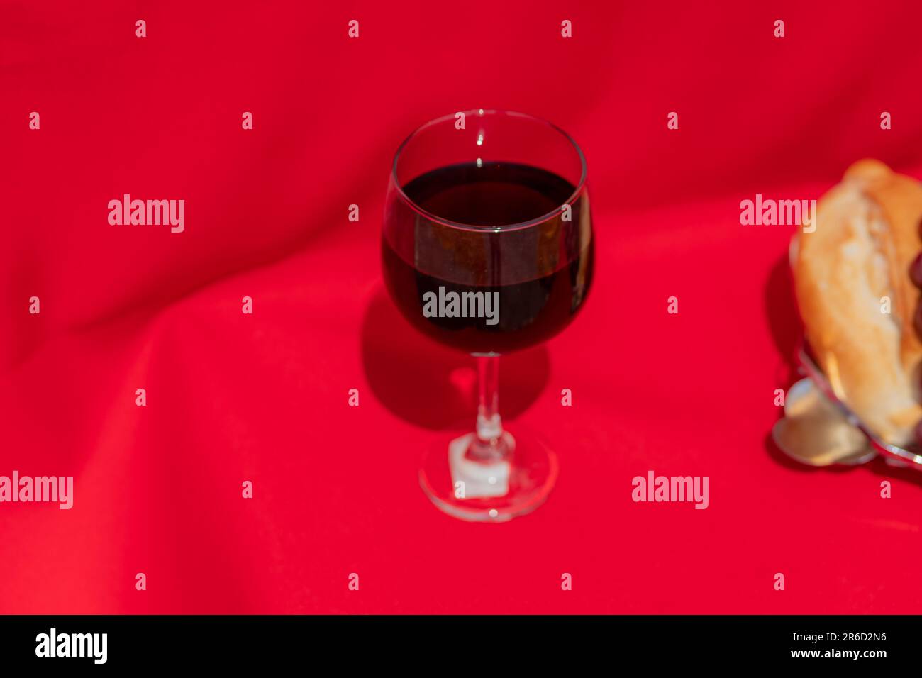 Wine glass, bread and grapes on red cloth in hard light. Symbolism of ...