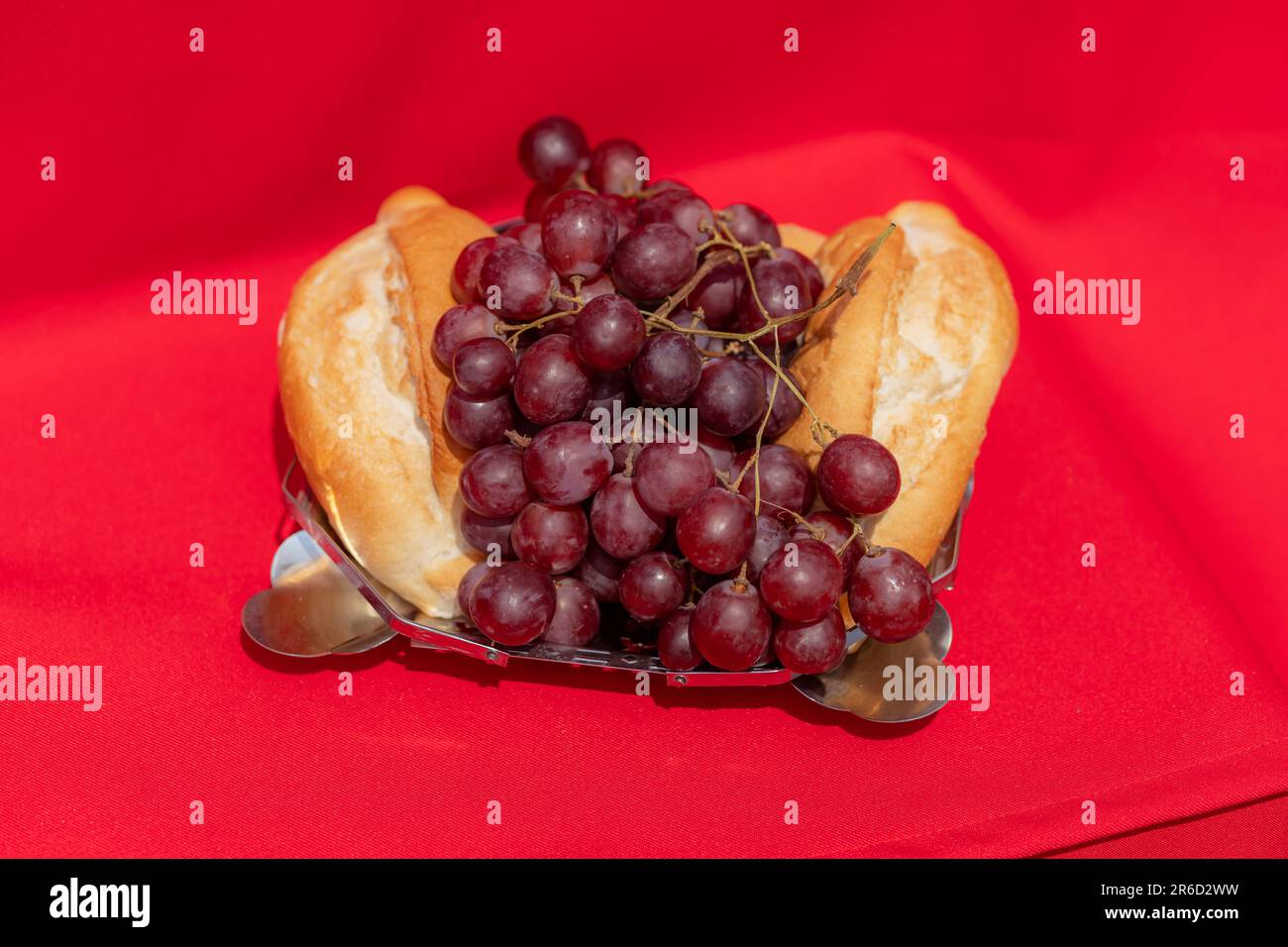 Wine glass, bread and grapes on red cloth in hard light. Symbolism of ...