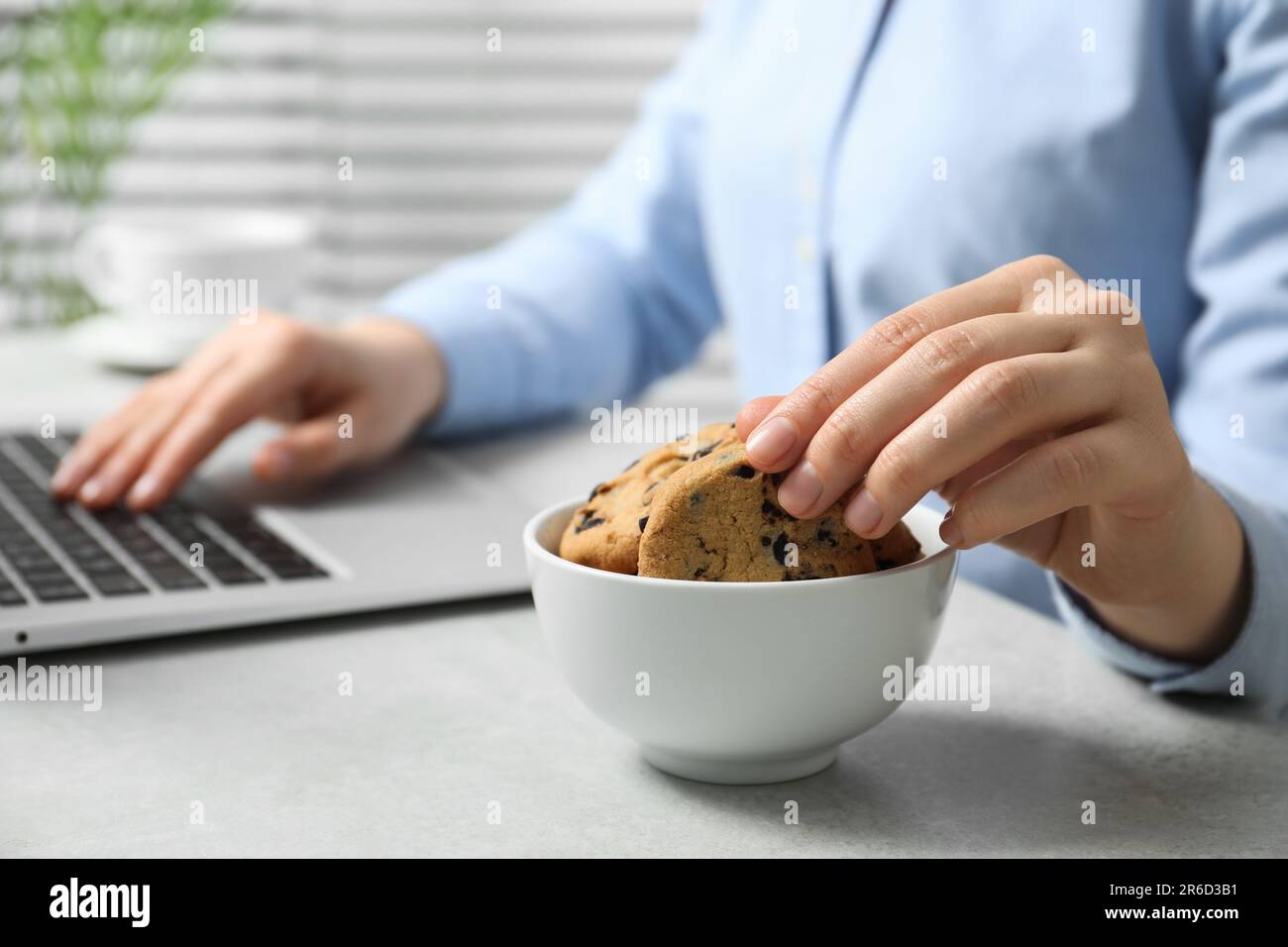 Office worker taking chocolate chip cookie from bowl at light gray ...