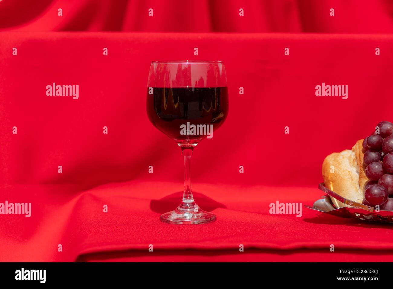 Wine glass, bread and grapes on red cloth in hard light. Symbolism of ...