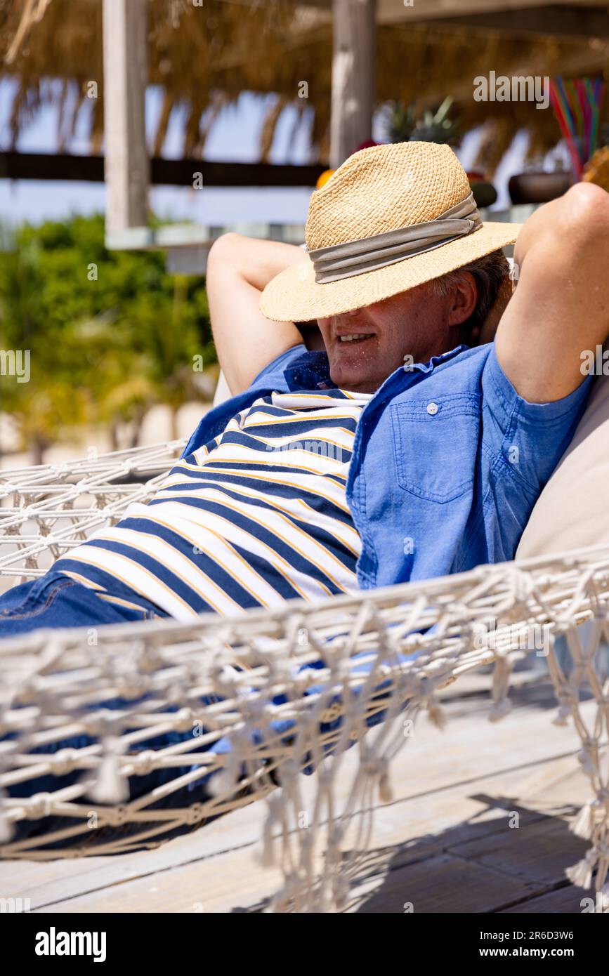 Caucasian senior man with hat on face and hands behind head sleeping on ...