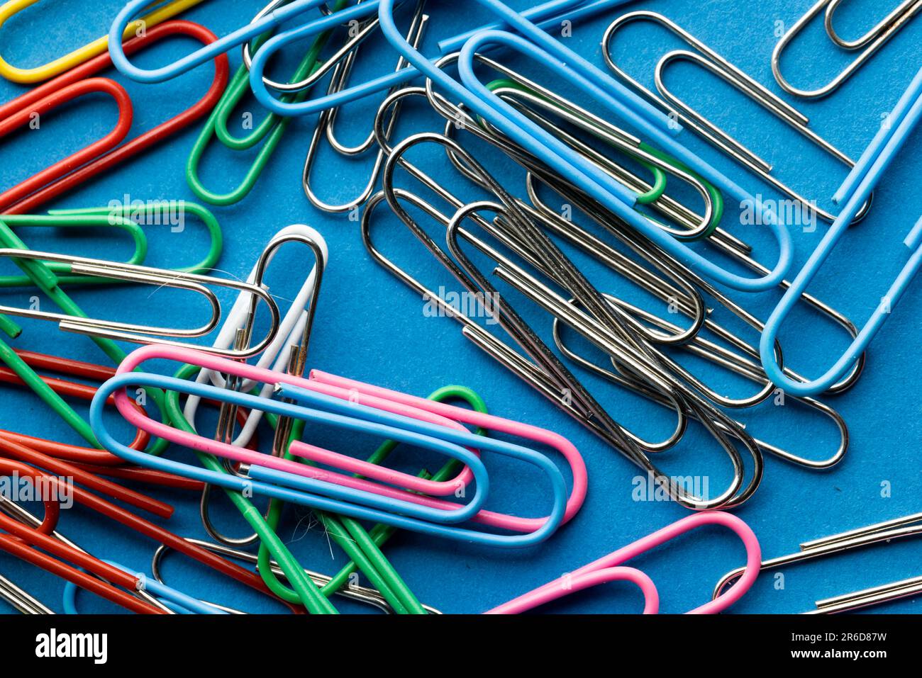 Close up of stack of multi coloured paper clips on blue background ...