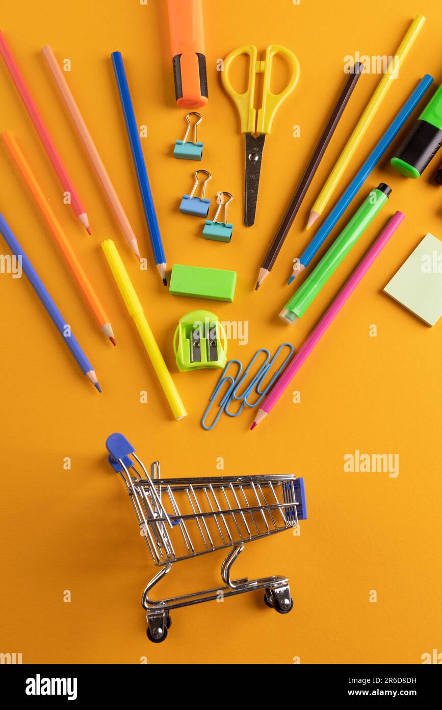 Close up of miniature shopping trolley with school materials on orange ...
