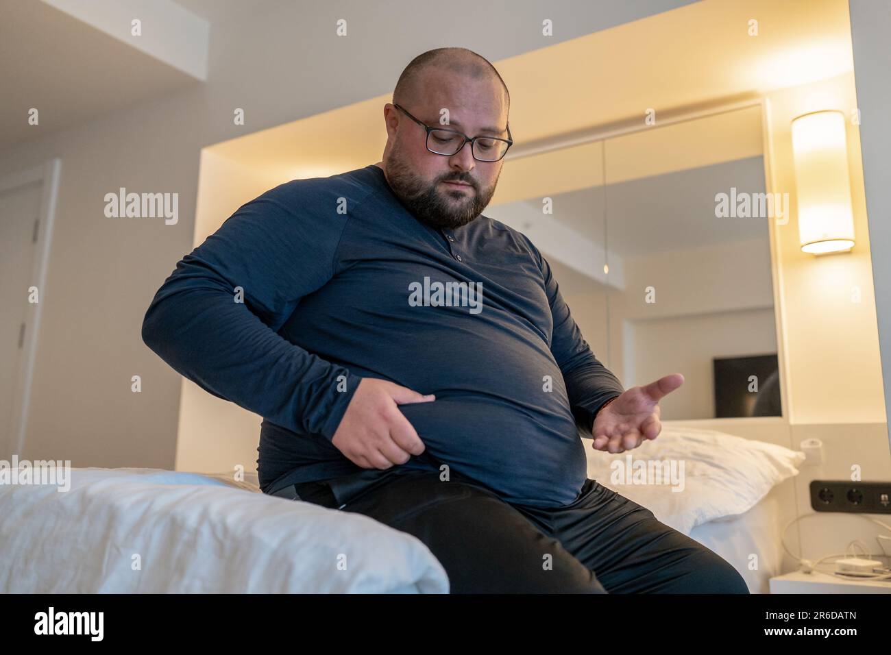 Huge man suffering from extra weight touching stomach sitting on bed in ...