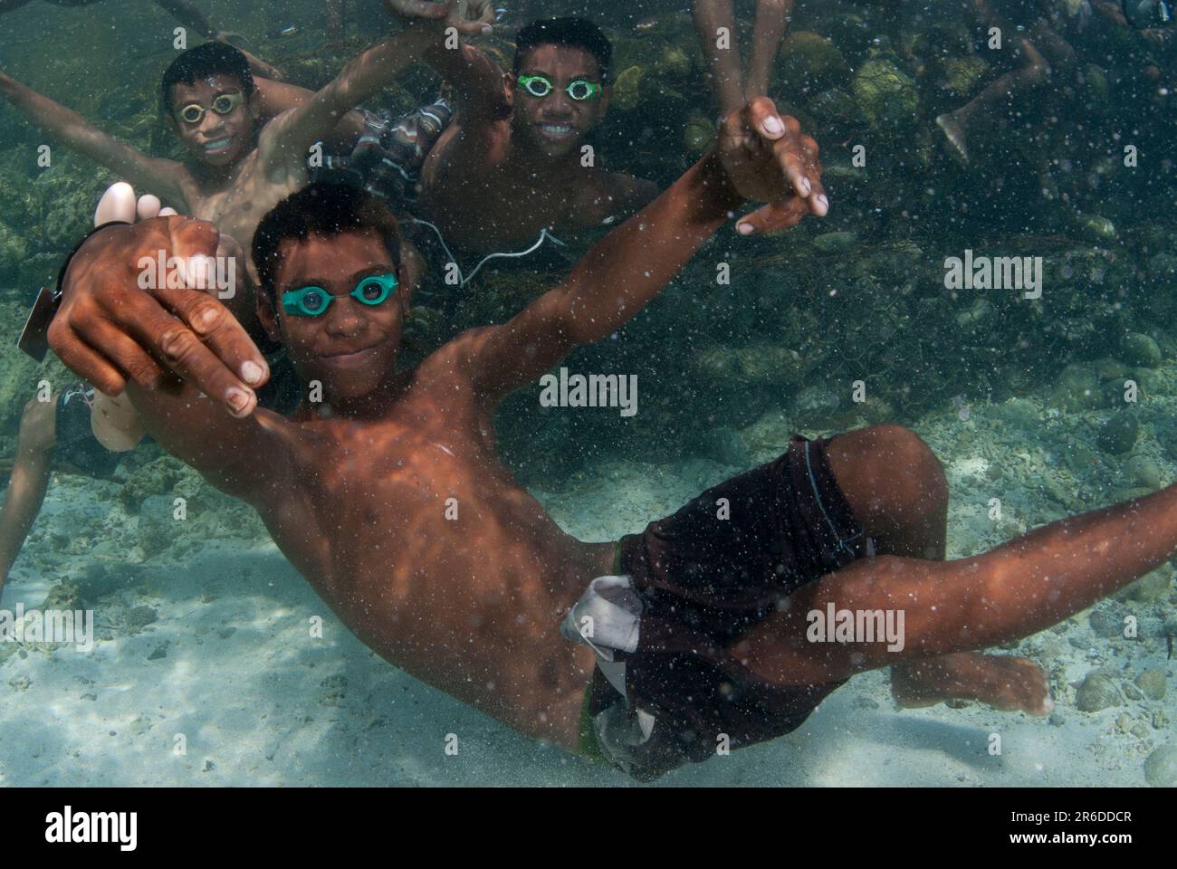 Boys with goggles underwater and making hand signals, Pier, Reta Island ...