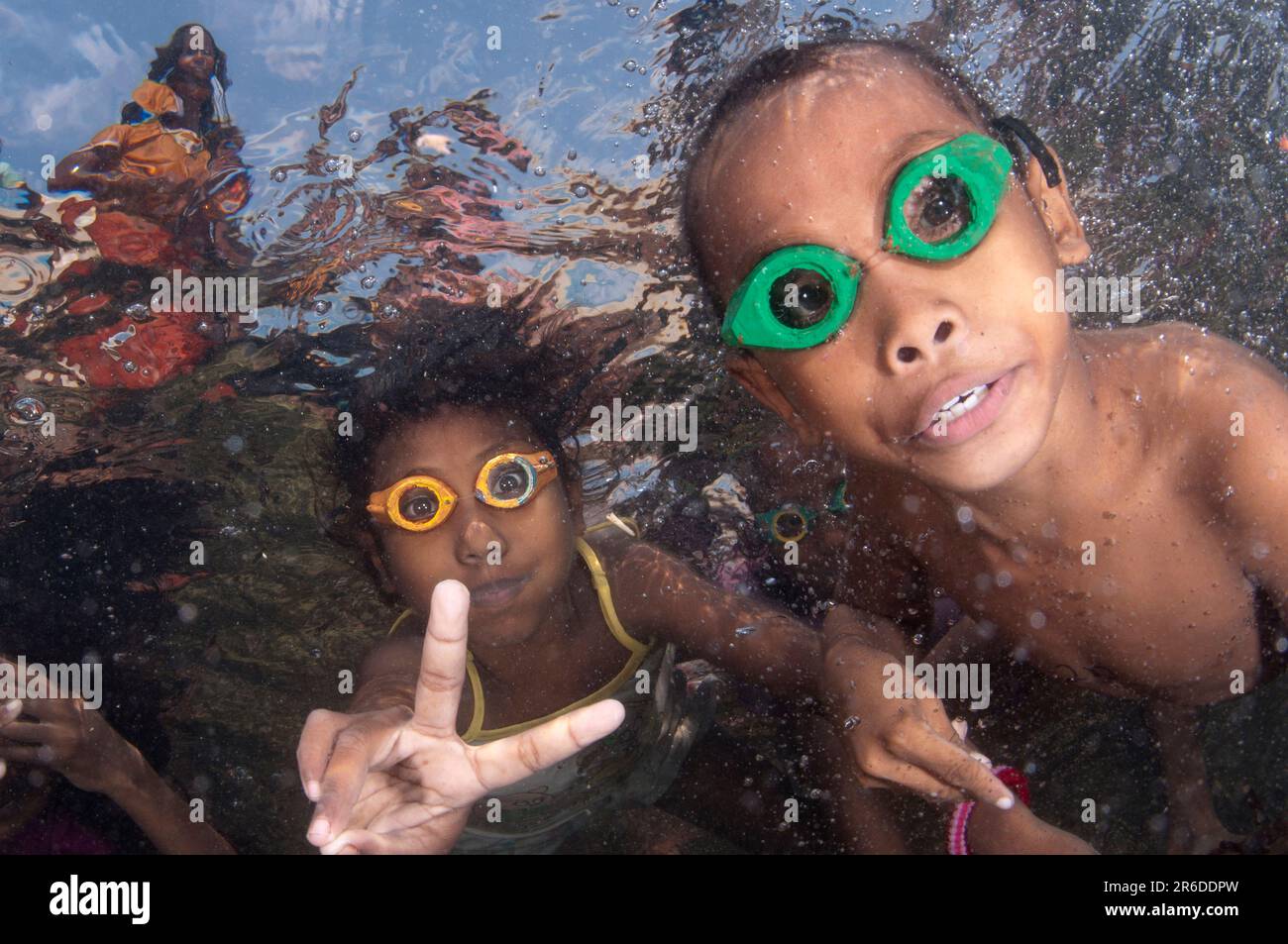 Kids with goggles underwater making hand signals with people on pier ...
