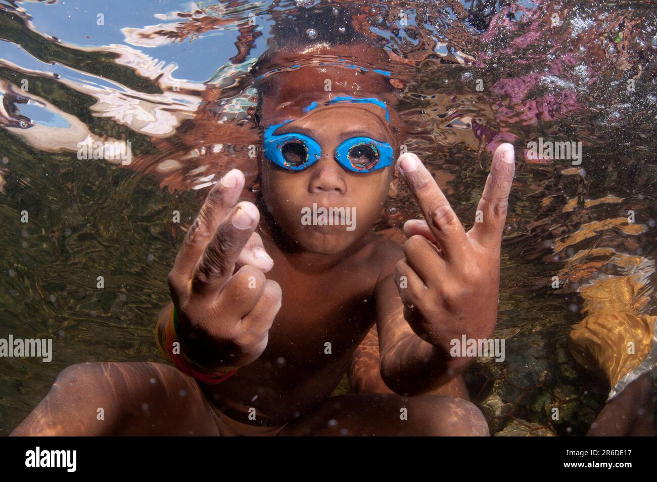 Boy with goggles underwater and making hand signals, Pier, Reta Island ...