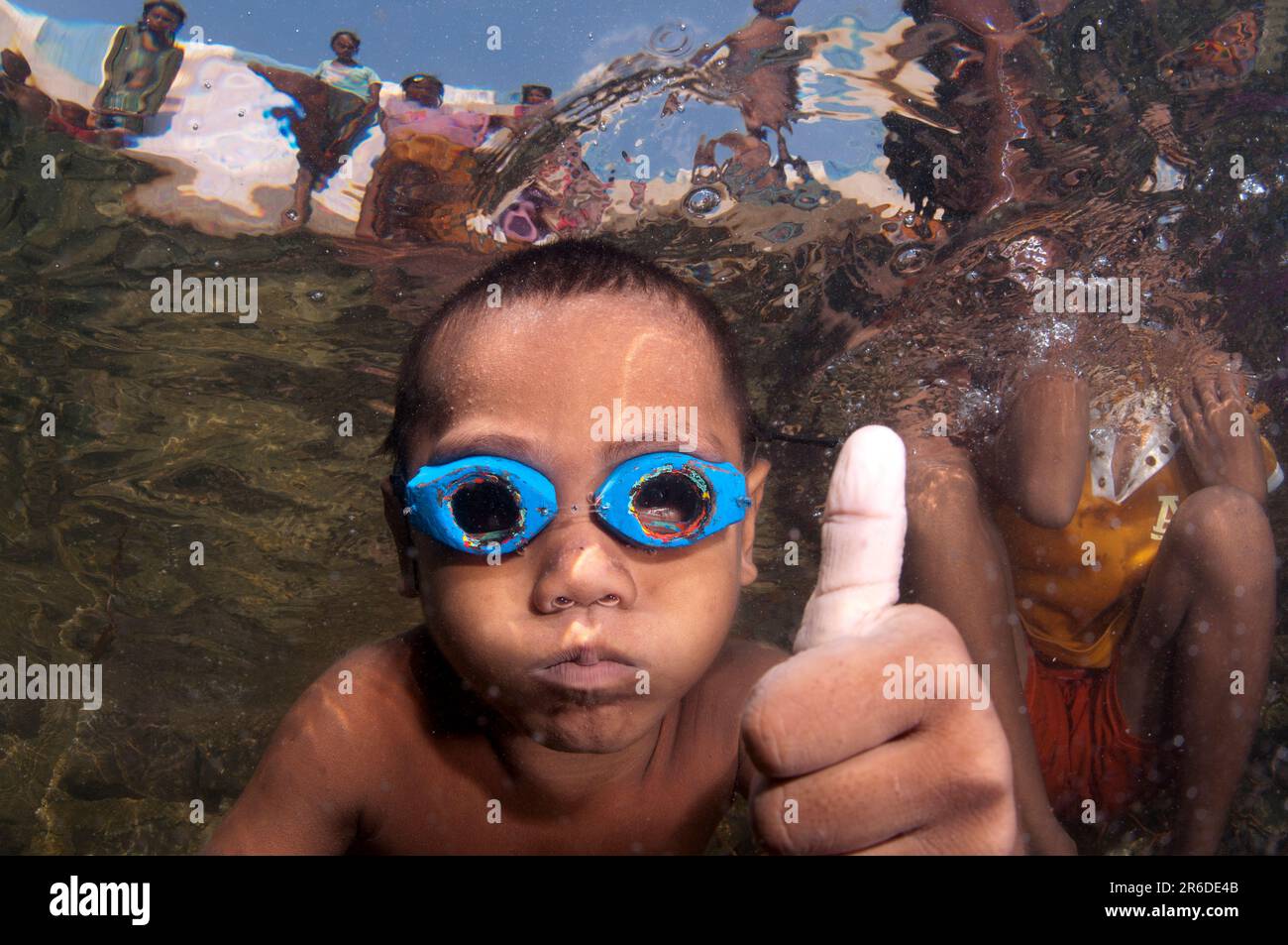 Boy with goggles underwater making hand signals with people on pier ...