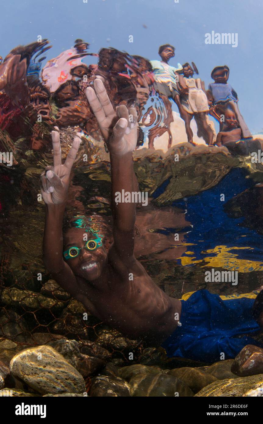 Boy with goggles underwater making hand signals with people on pier ...