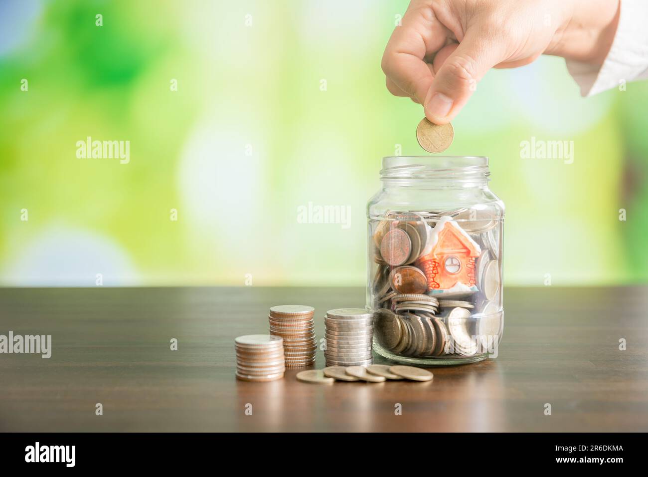 hand put money coins in glass of jar and green bokeh background ...