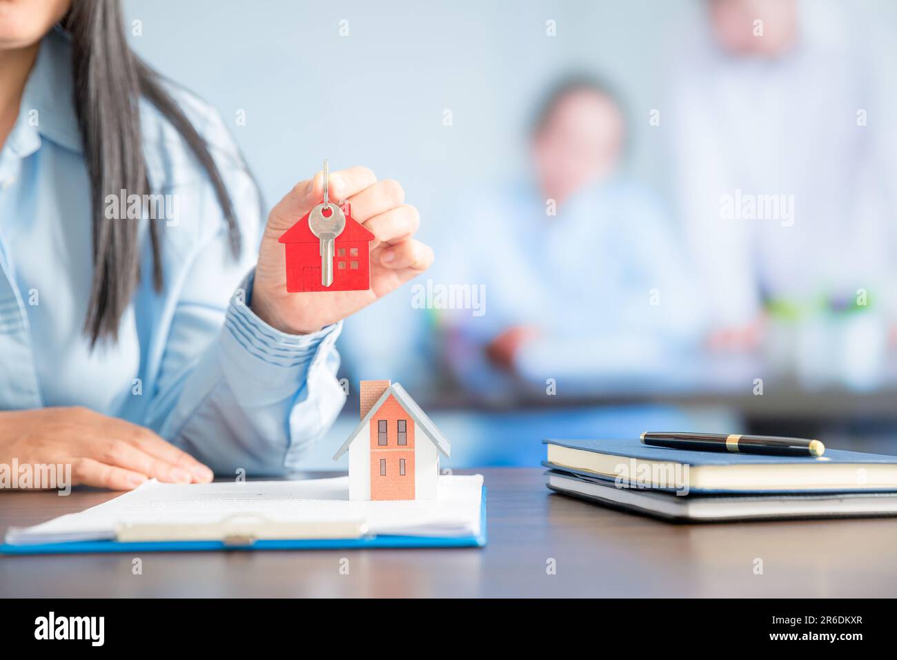 Real estate agent holding house key on table with house designs ...