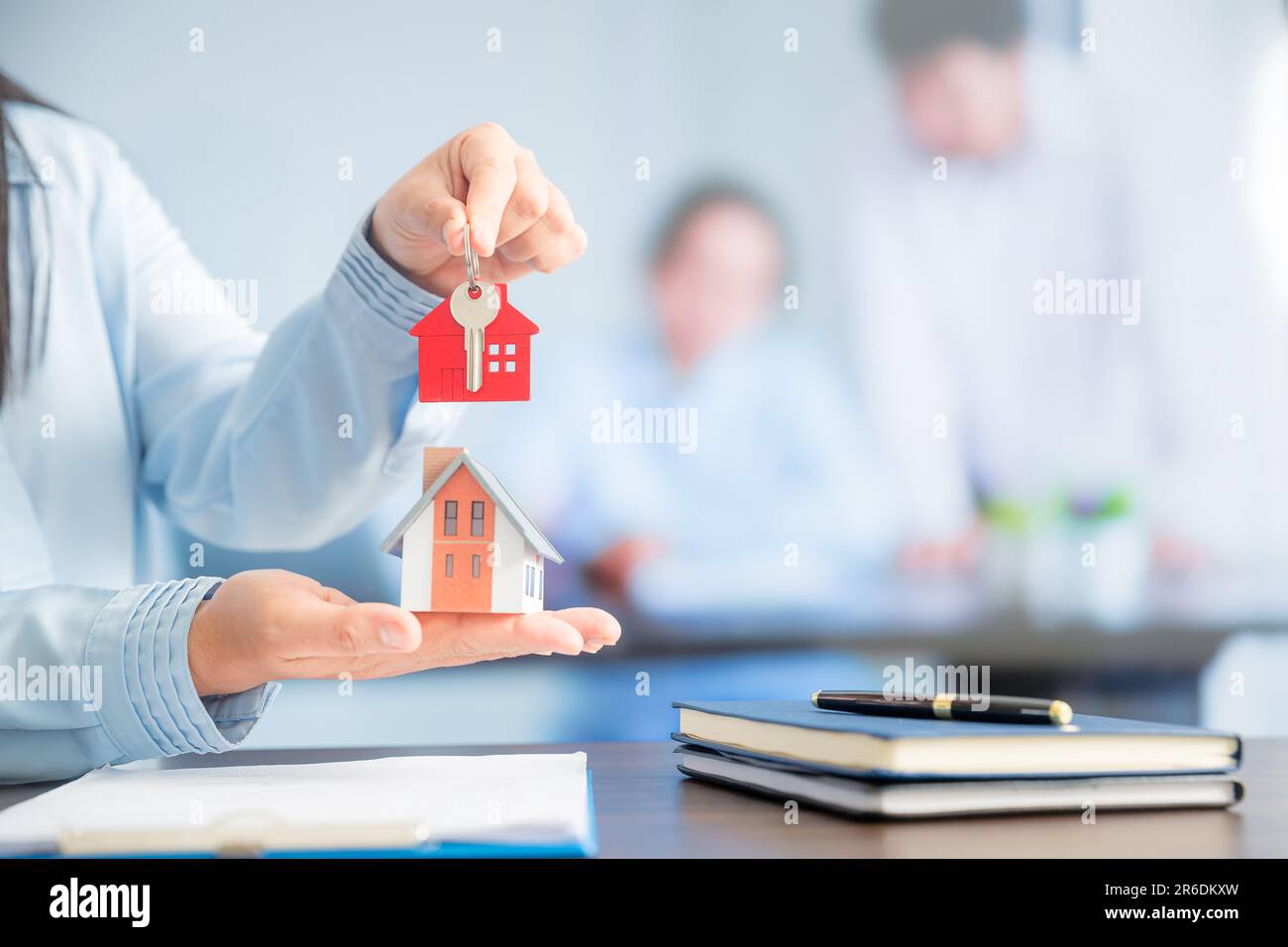 Real estate agent holding house key on table with house designs ...