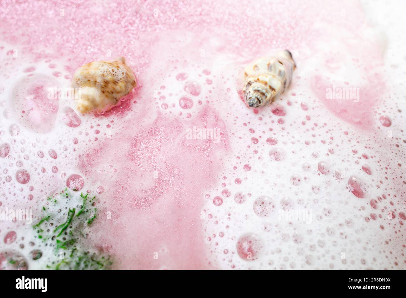 White foam, water and pink glittery sand with sea shells and weeds ...