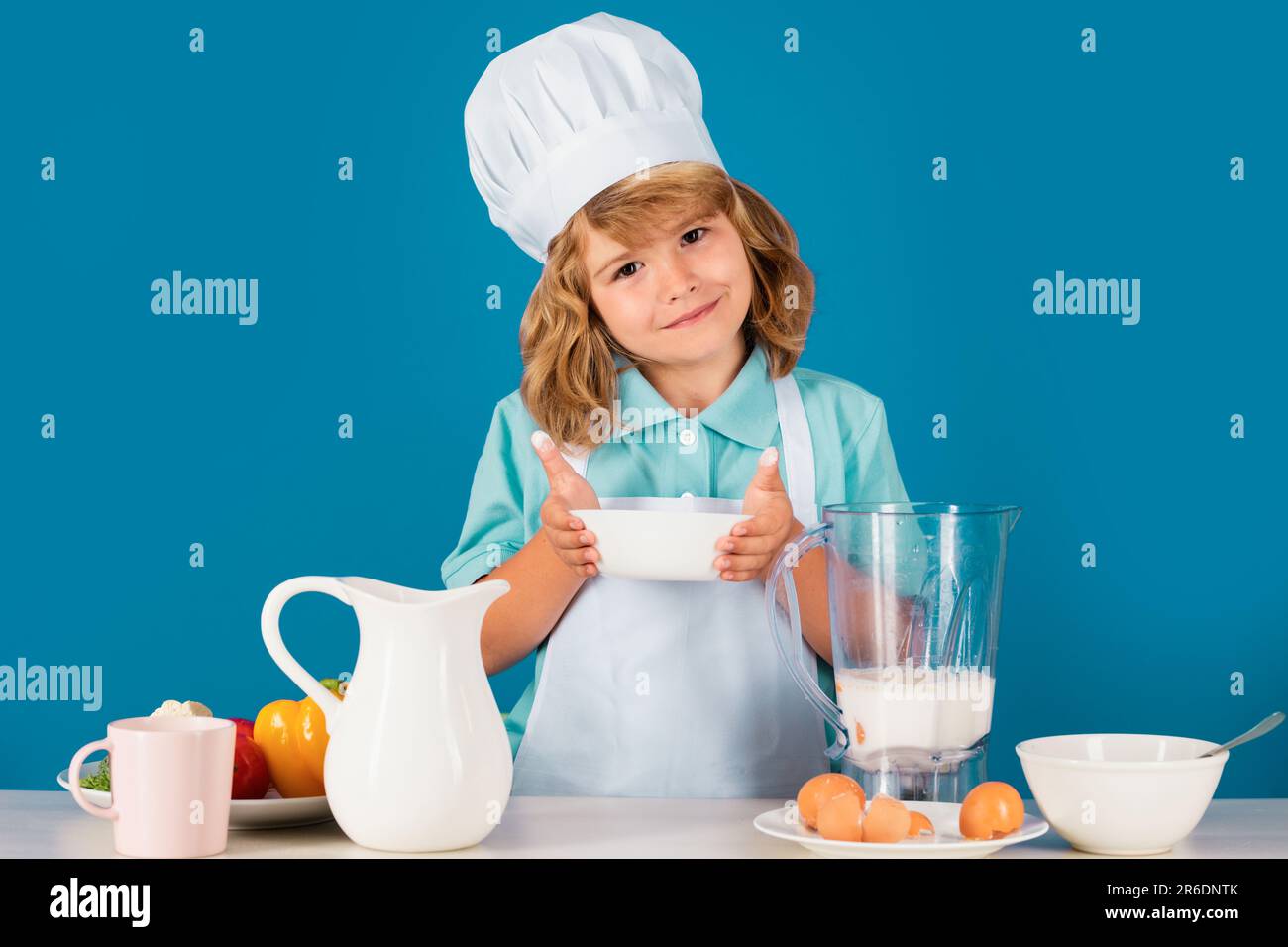 Child chef cook prepares food in isolated blue studio background. Kids ...