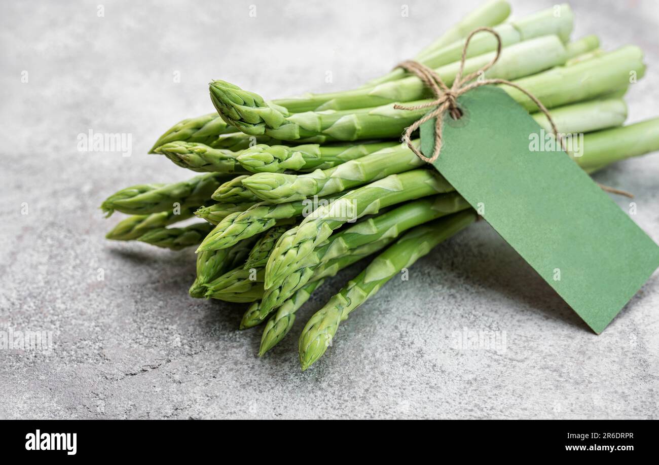 Fresh green asparagus with empty tag on grey concrete background. Flat ...