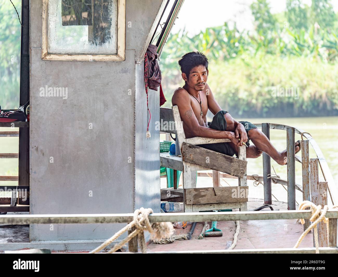 Ferry skipper wearing a longyi and smoking a typical Burmese cigarette ...