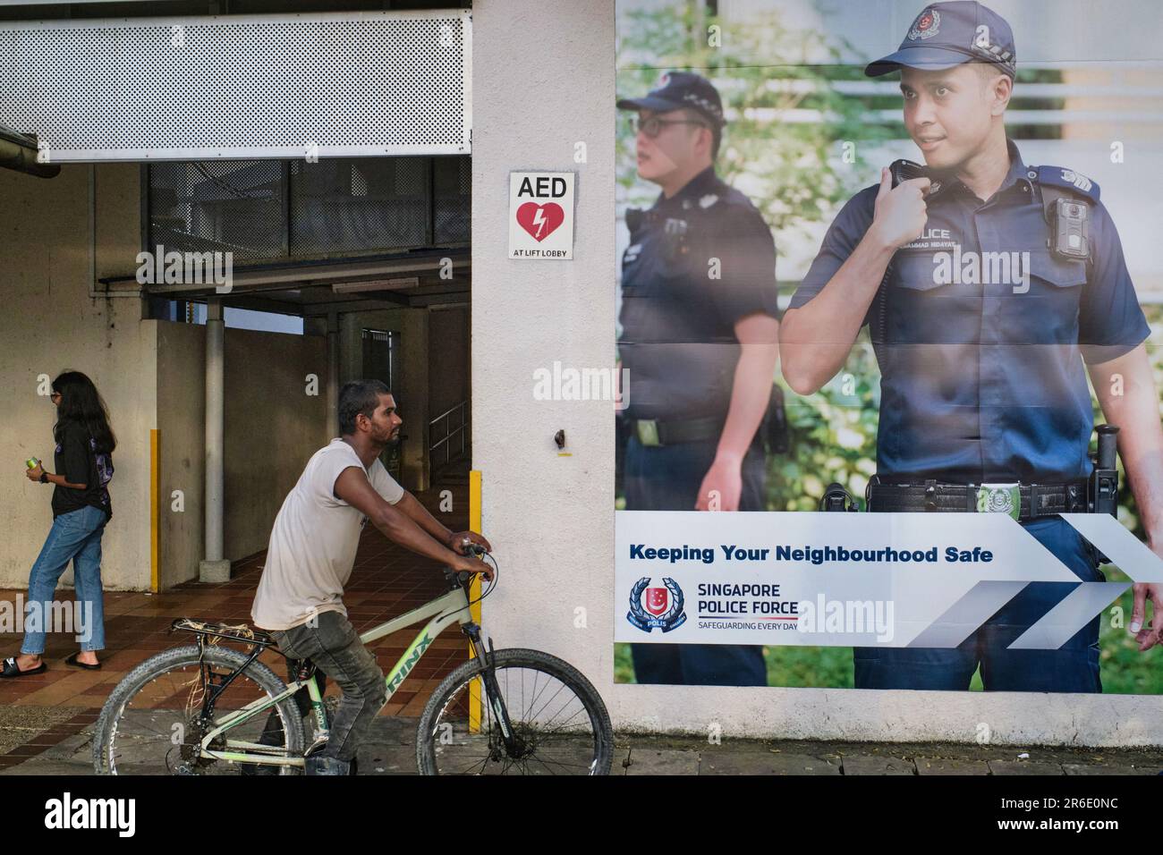 A South Asian worker cycles past a large advertisement or awareness ...