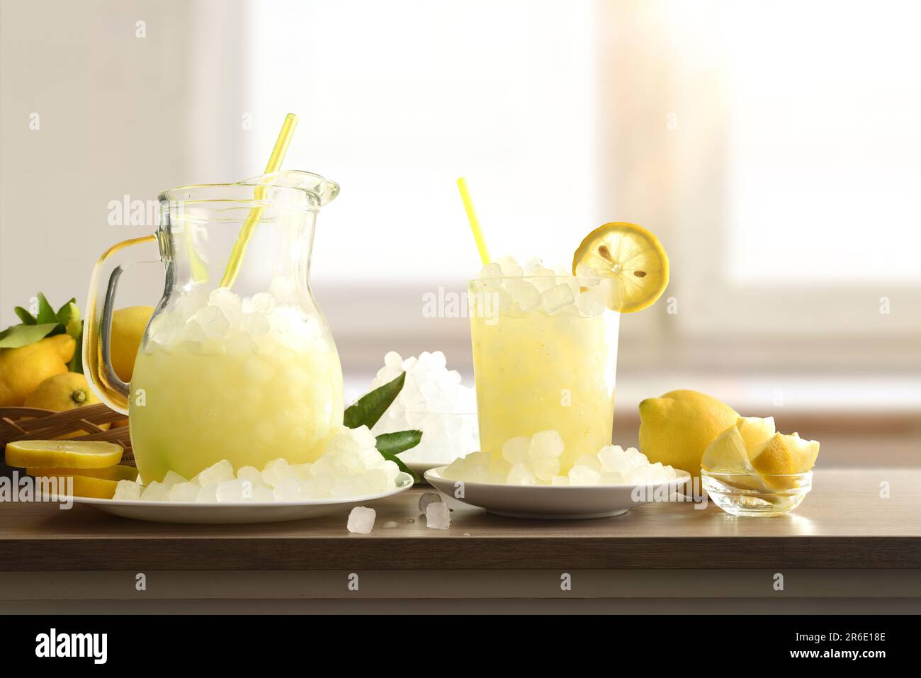 Lemonade with ice in a pitcher and glass on a wooden bench with fruit ...