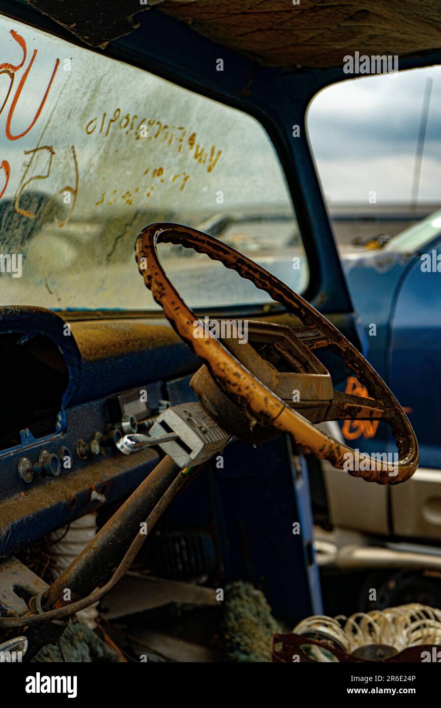 A rusty, battered car in a junk yard, its body dented and paint faded ...