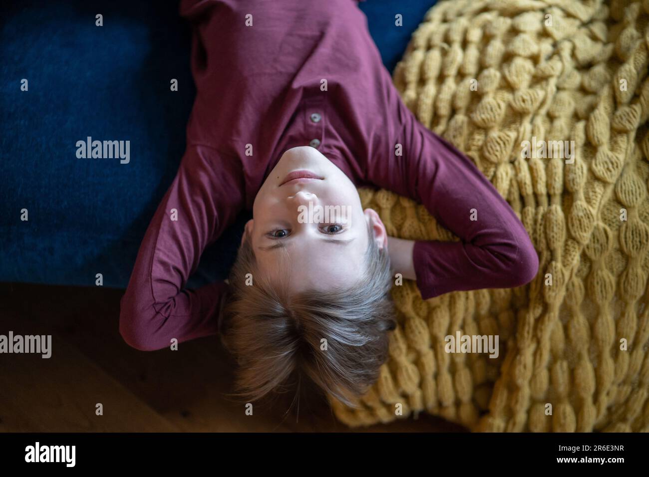 Portrait teenage boy lying on sofa upside down with hands behind head ...