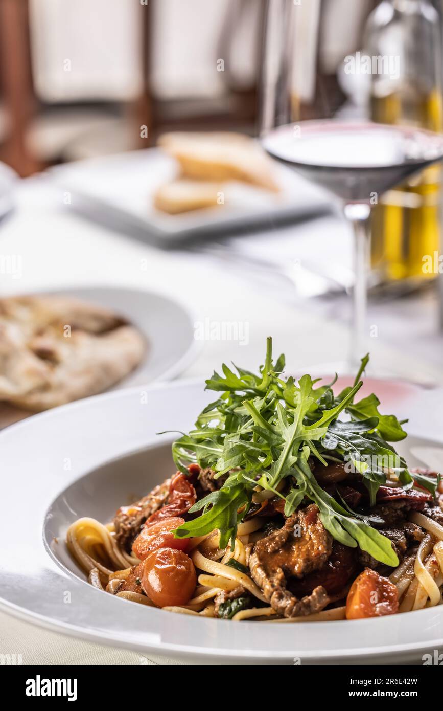 Detail of meat linguine with tomatoes and rocket served with wine on a ...
