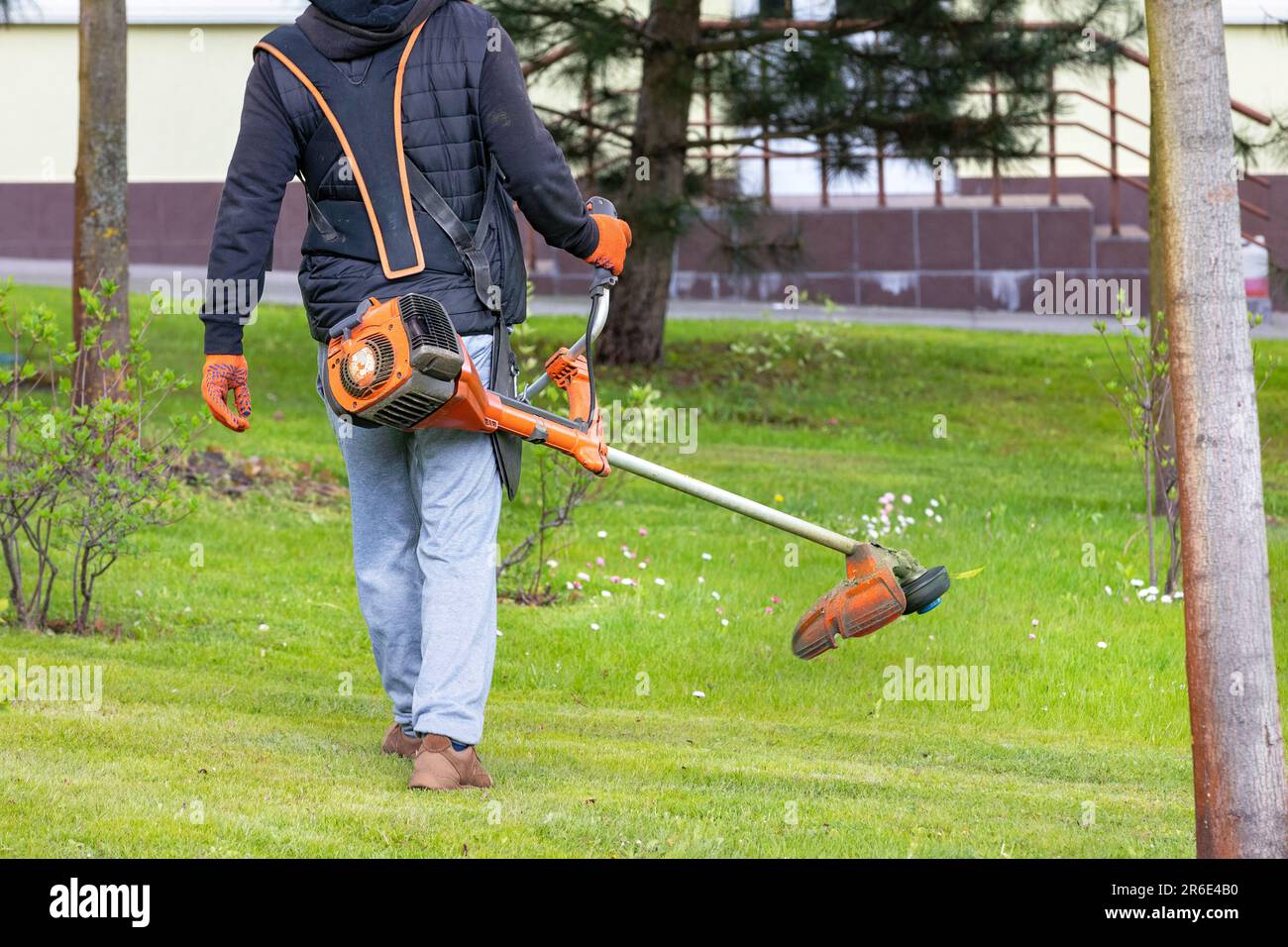 Petrol trimmer on the shoulder suspension of a gardener moving through ...
