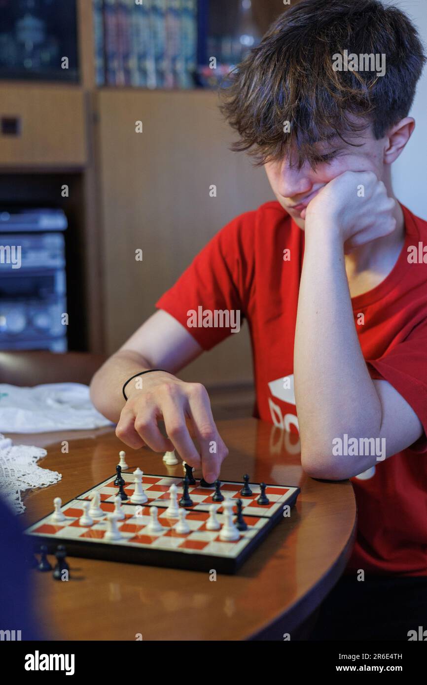 Concentrated Boy with his Hand resting on his Cheek moving a Pawn on a ...