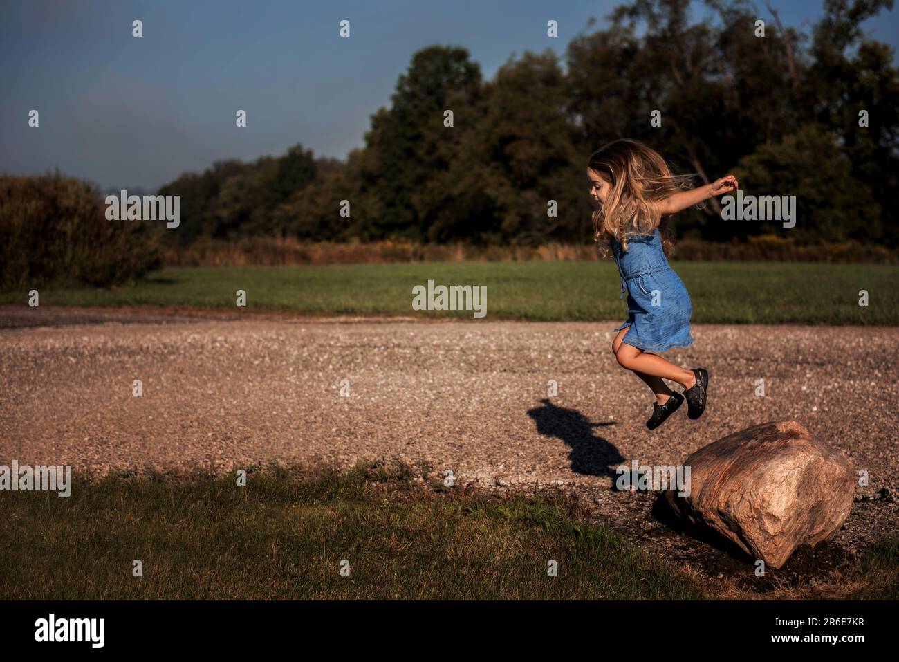 You girl jumping off rock in sunny field Stock Photo - Alamy