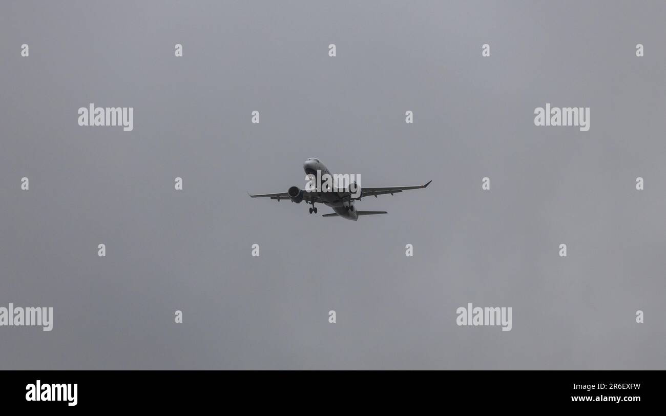 A JetBlue Airbus A220 aircraft flying through the sky on a grey cloudy ...