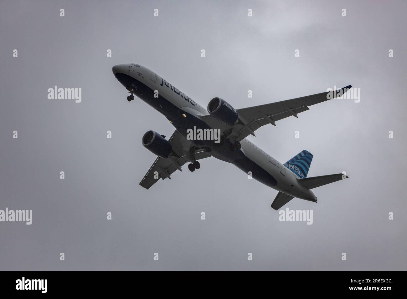 A JetBlue Airbus A220 aircraft flying through the sky on a grey cloudy ...