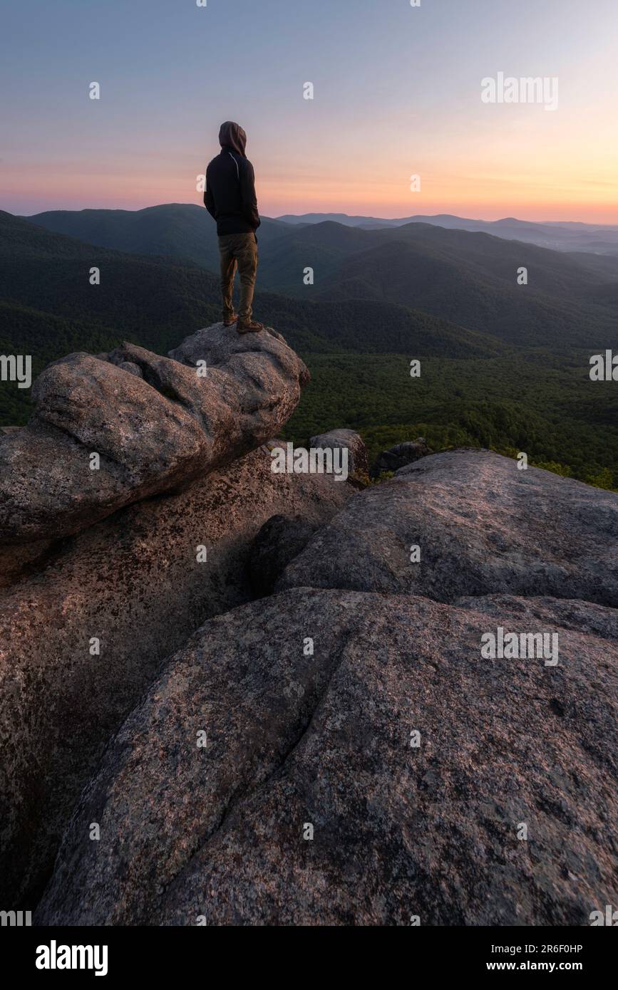 A hiker poses at sunrise atop a boulder on the summit of Old Rag in ...