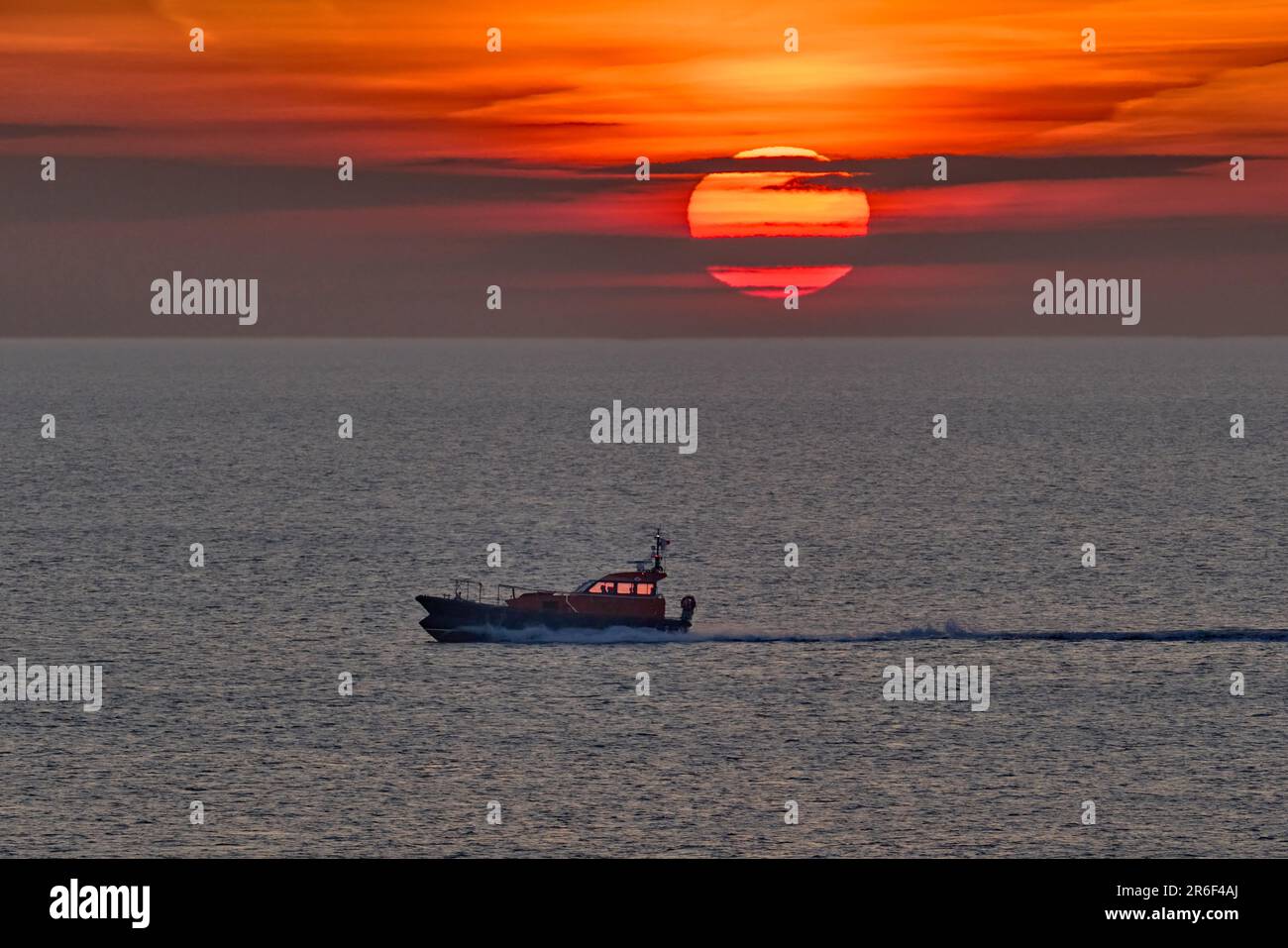 A photograph of a fast boat in the sea under a warm orange sunrise ...