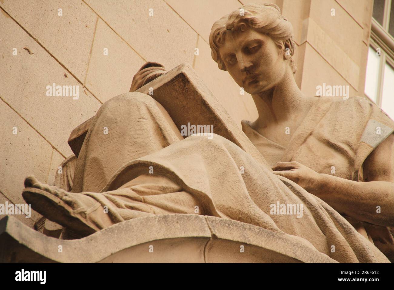 A stone statue of a figure holding a book on a ledge of an old building ...