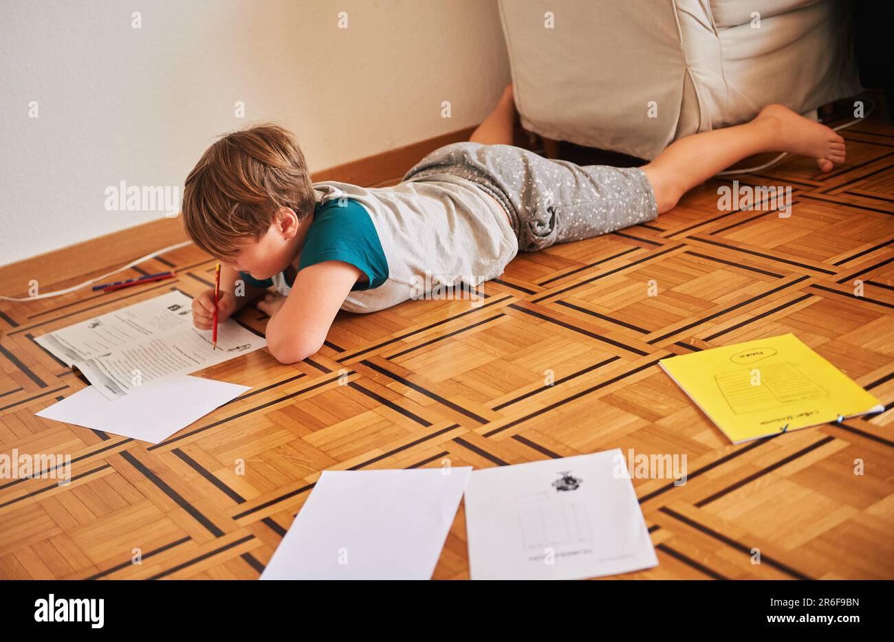 Funny kid boy doing school homework, lying on the floor, homeschooling ...
