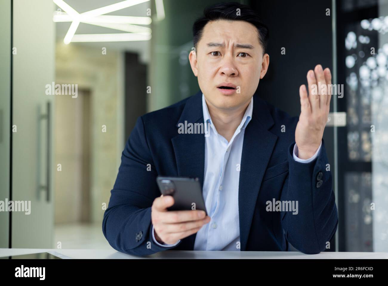 Dissatisfied Asian looking at camera, man inside office holding phone ...