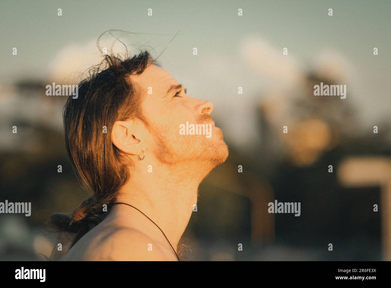 A Caucasian male adult standing outdoors, looking up into the sky with his head tilted back ...