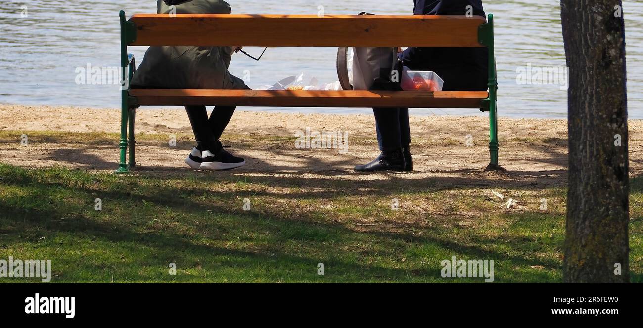 Two adults enjoying a sunny day outdoors, seated side-by-side on a park ...