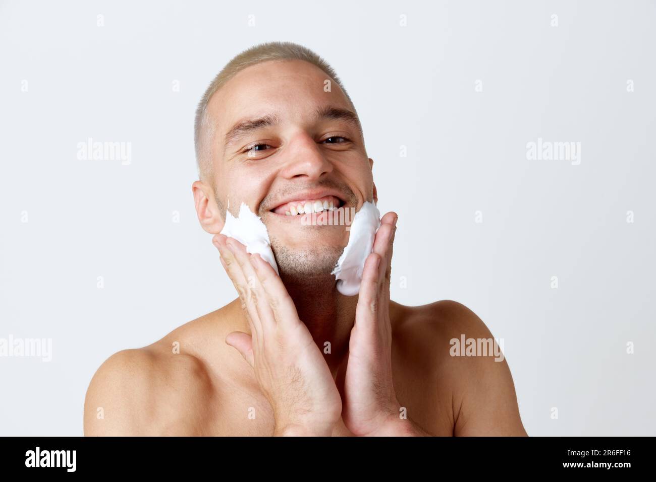 Morning routine. Portrait of smiling young man applying shaving gel ...