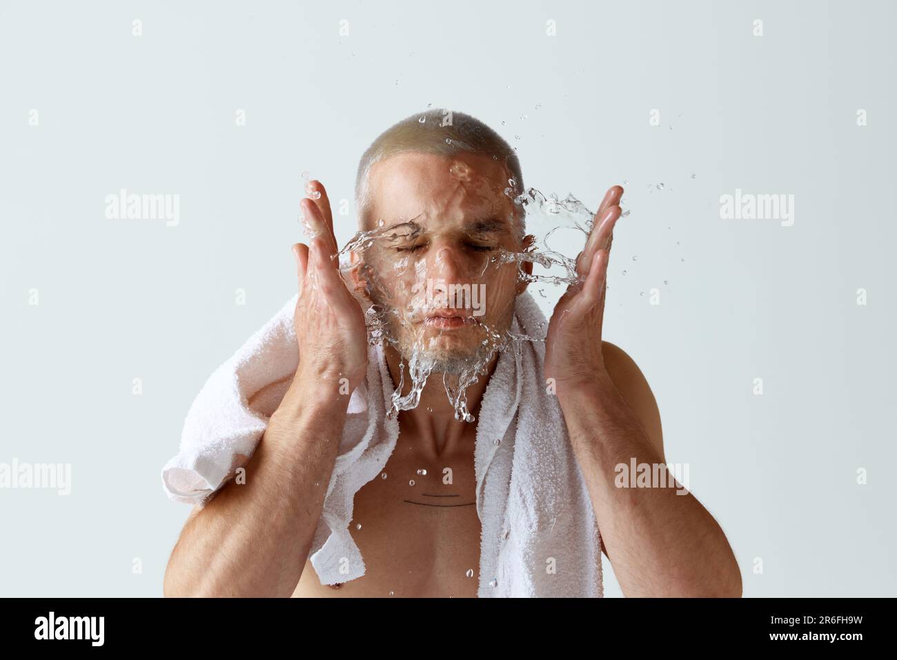 Morning hygiene. Handsome young man washing his face, taking care after skin against white ...