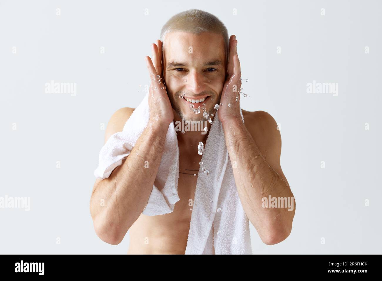Morning hygiene. Handsome, smiling, young man washing his face, taking care after skin against ...