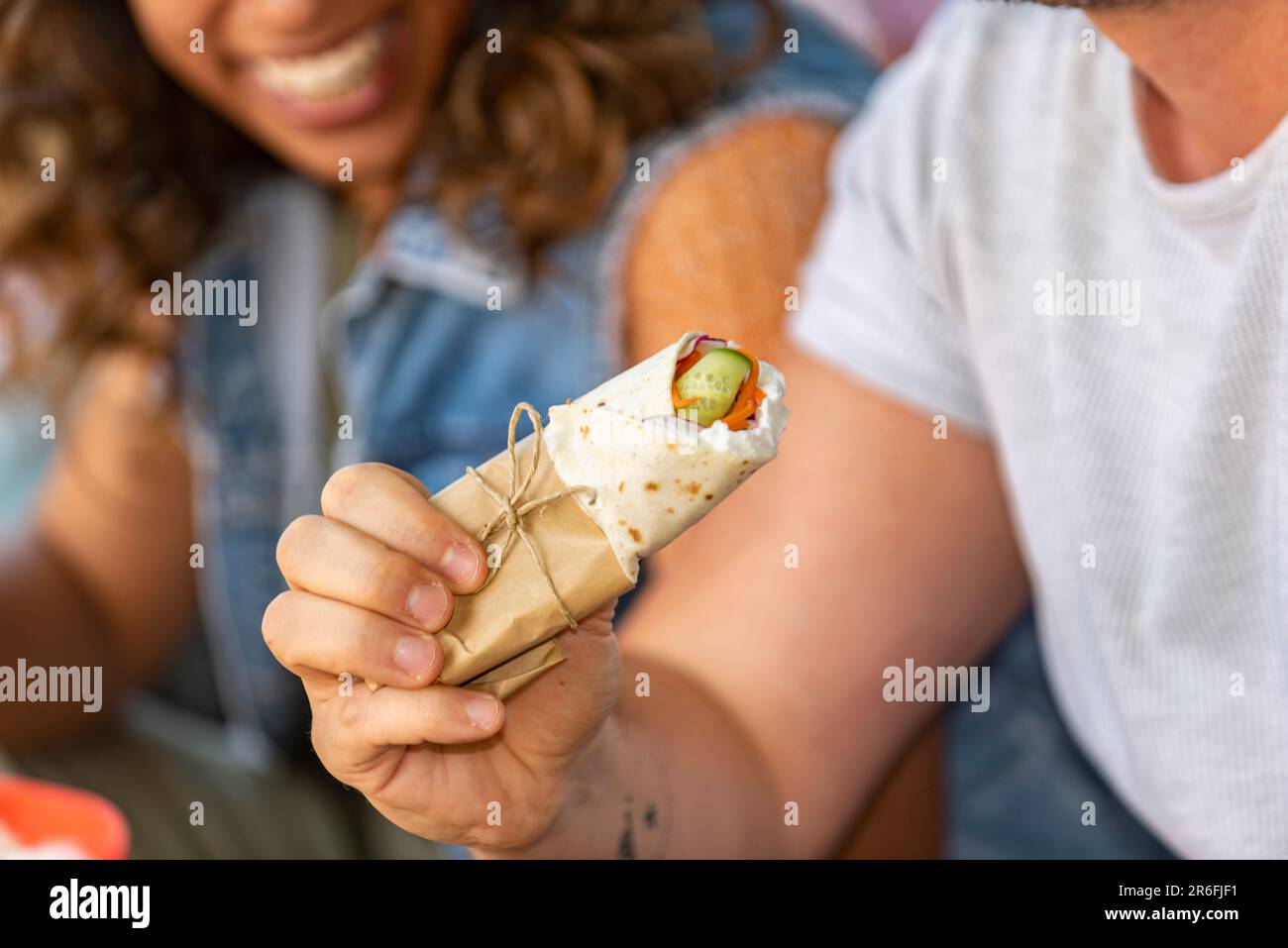 man is holding a vegan burrito in his hand beside a woman having good ...