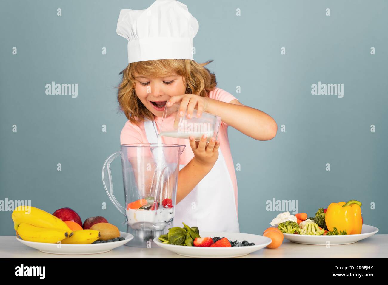 Kid boy in chef hat and apron cooking milk shake smoothie. Little cook ...