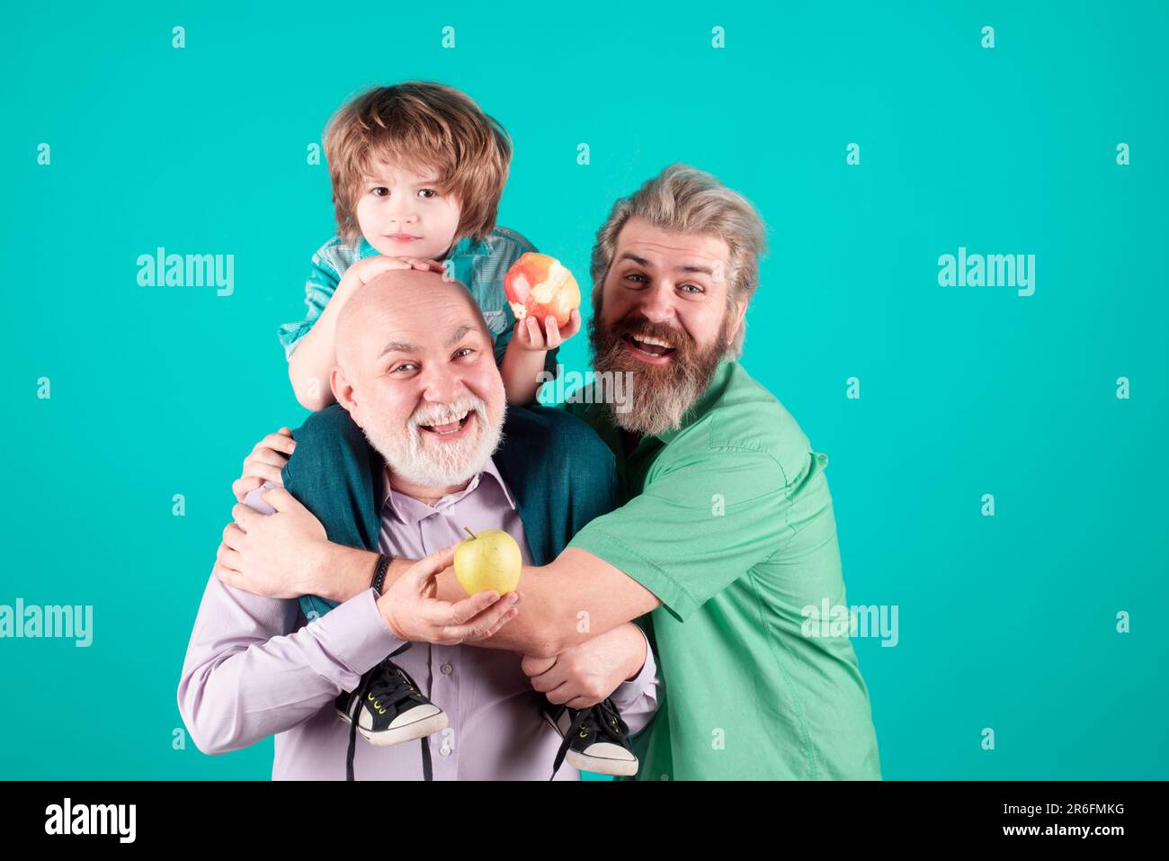 Grandfather father and on hugging and eating apple. Men in different ...