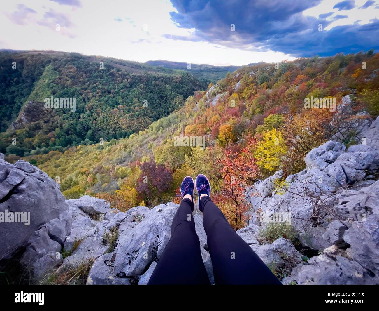 A young adult sitting on a large rock over a scenic landscape of ...