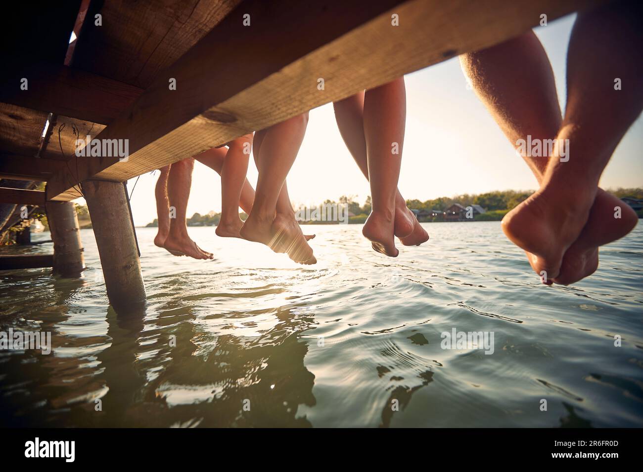 friends together sitting on the dock and enjoying dangling legs in the ...