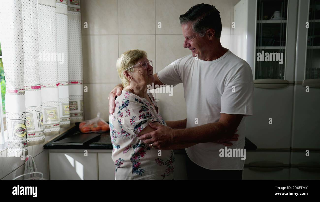 Adult son embracing elderly mother standing at home kitchen. Authentic ...